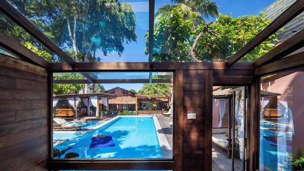 Estrutura de vidro com moldura de madeira e vista para uma piscina ao ar livre, um deck de madeira e vegetação ao redor.