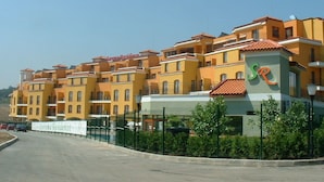 Fileira de edifícios amarelos com varandas, uma placa com a inscrição 'Serena Residence' e um logotipo verde à direita.