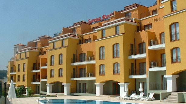 Um hotel com piscina, várias varandas e céu claro.
