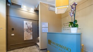Uma área de recepção com balcão azul exibindo "Fororomano Luxury Suites" e uma orquídea em vaso.
