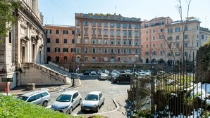 Vista da rua com carros estacionados, uma escadaria de pedra e edifícios de vários andares com arquitetura clássica.
