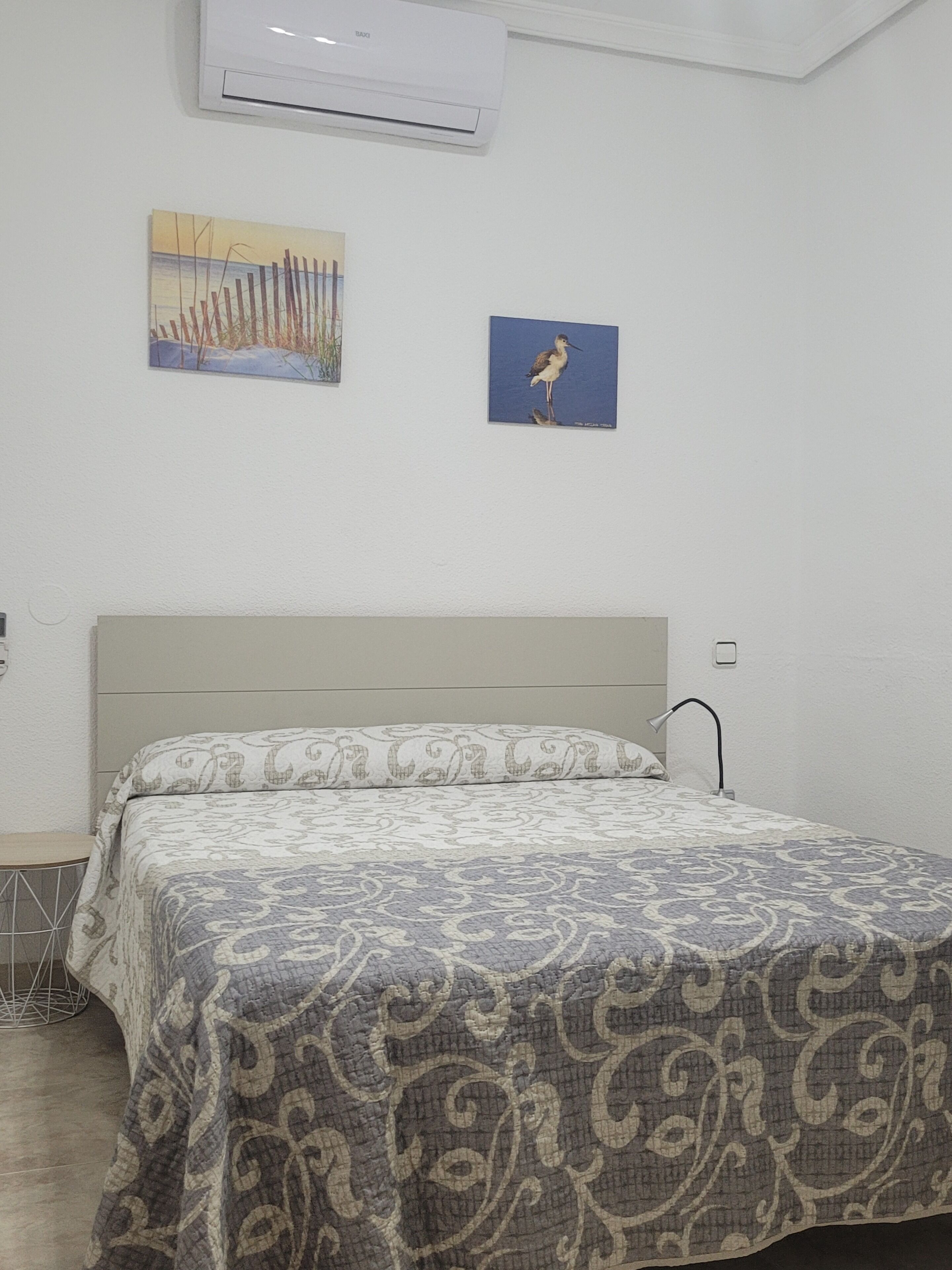 Quarto com cama, ar condicionado fixado na parede e duas imagens emolduradas.