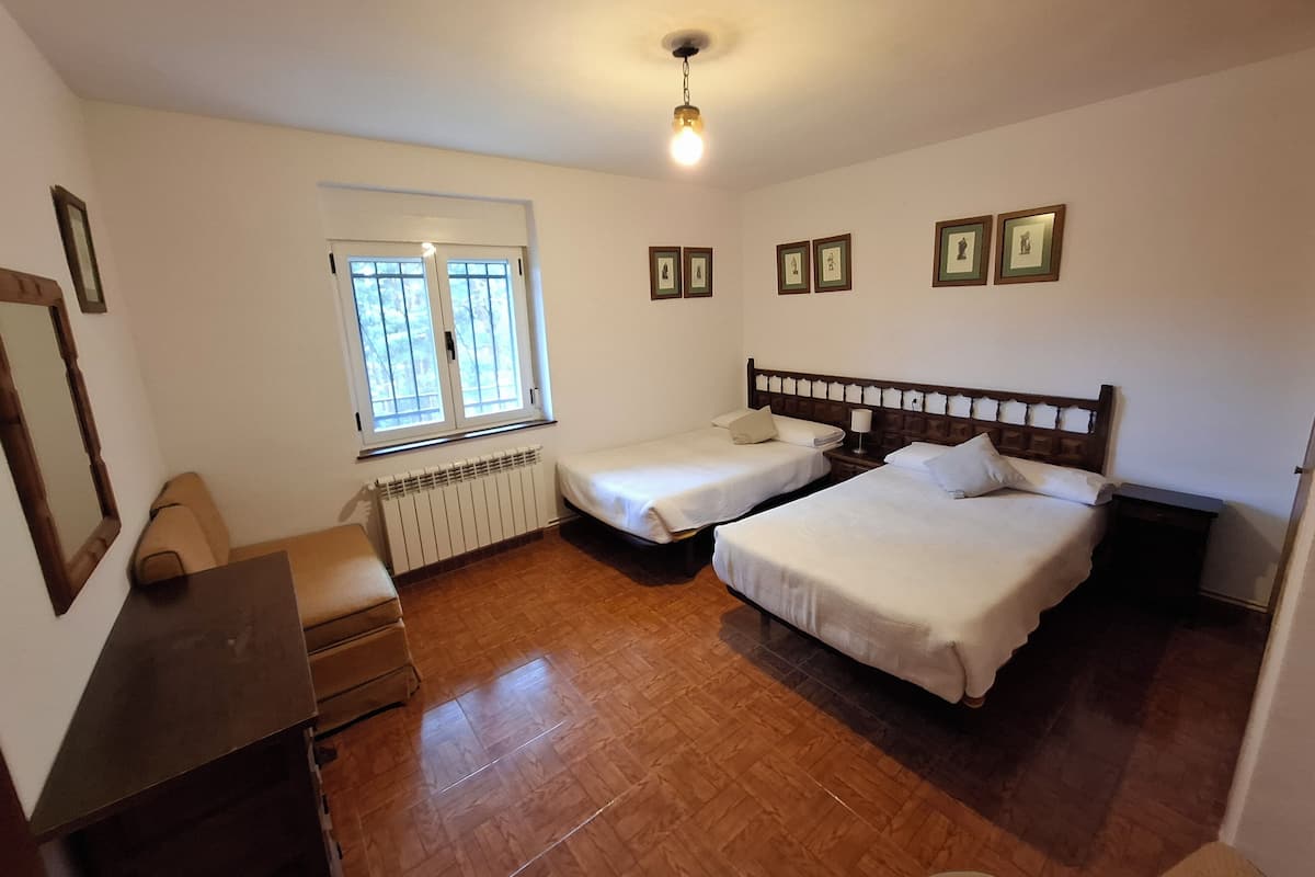 Quarto com duas camas, um radiador, uma janela e uma escrivaninha.