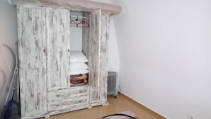 Um guarda-roupa branco rústico, com várias gavetas e uma barra para pendurar roupas.