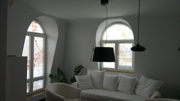 Quarto com sofá branco, duas janelas em arco e uma luminária pendente.