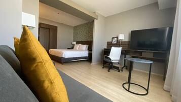 Quarto de hotel moderno com cama, televisão, escrivaninha e sofá.