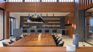 Uma sala de jantar moderna com uma mesa de madeira comprida, cadeiras pretas e uma luminária pendente central.