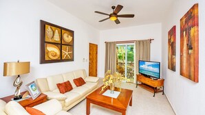 Uma sala de estar com sofá, mesa de centro, TV e obras de arte nas paredes.
