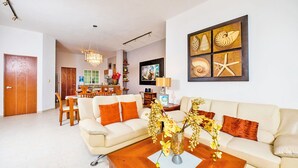 Sala de estar com sofá, mesa de centro e objetos decorativos. Ao fundo, área de jantar com cadeiras e mesa.