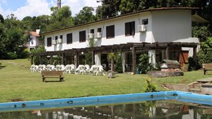 Um edifício branco com várias janelas e aparelhos de ar condicionado, um gramado, uma piscina e móveis para área externa.