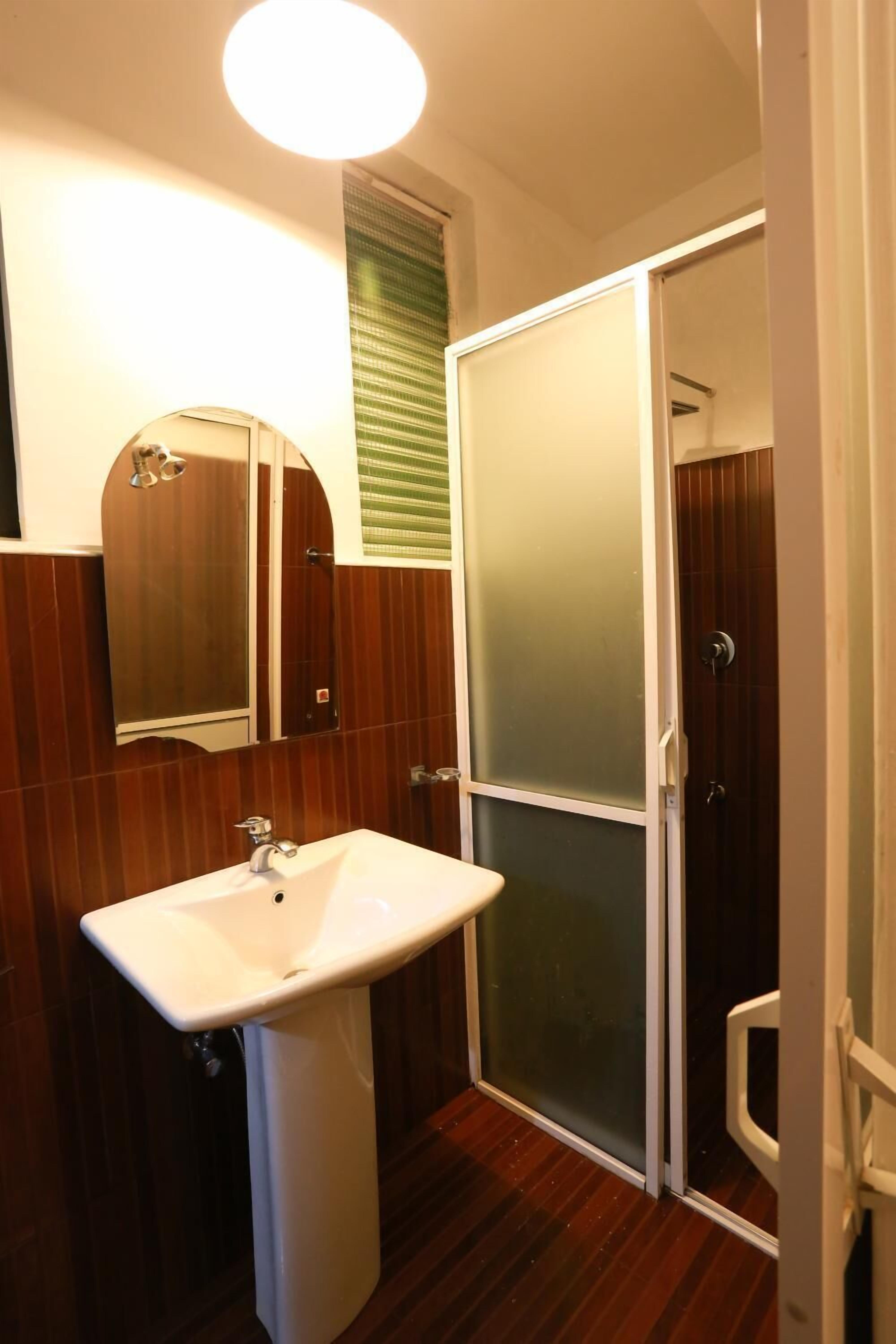 Casa de banho com lavatório branco, espelho e porta de chuveiro em vidro deslizante.