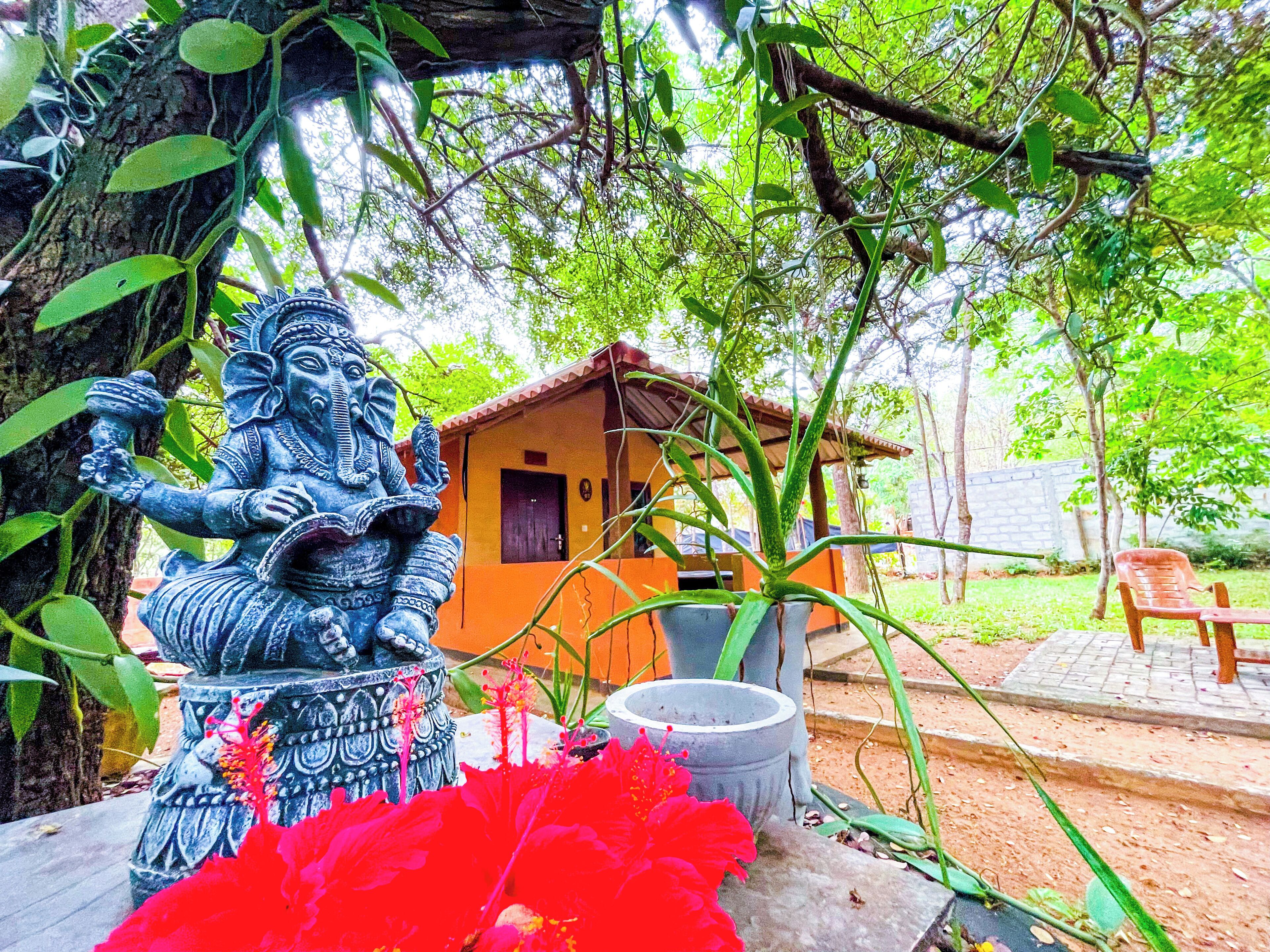 Uma estátua de divindade, uma casa pequena e uma flor vermelha em um jardim.