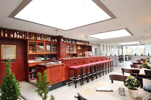 Uma área de bar com armários de madeira, banquetas vermelhas e um balcão longo.