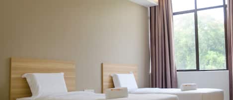 Quarto de hotel com duas camas, uma janela grande e piso de madeira.