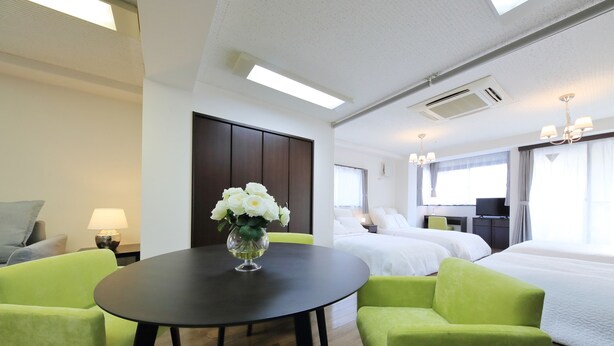 Quarto de hotel com cama, escrivaninha, cadeira, mesa com um vaso de flores e janela com cortinas.