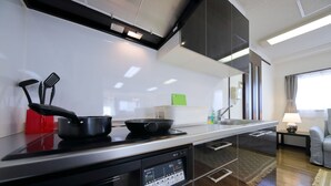 Cozinha moderna com fogão embutido, micro-ondas e máquina de café. Há um descanso de panela vermelho na bancada e uma tábua de corte verde.