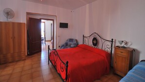 Um quarto com uma cama, um guarda-roupa de madeira, uma mesa de cabeceira e um ventilador de teto.