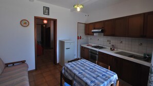Uma cozinha compacta com armários de madeira, geladeira e uma mesa de jantar com toalha de mesa estampada.