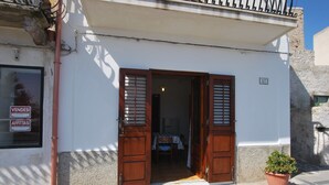 Edifício com fachada branca, porta de madeira e planta em vaso na frente.