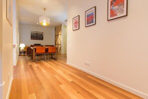 Um corredor com piso de madeira, área de jantar com cadeiras laranja e obras de arte emolduradas nas paredes.