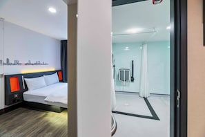Quarto de hotel com cama, painel de parede com vista urbana, chuveiro e porta de vidro.