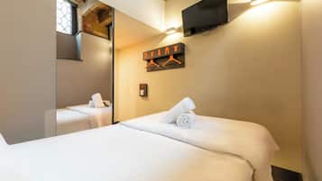 Quarto de hotel com cama, espelho, televisão presa à parede e porta-toalhas fixado na parede.