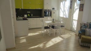Cozinha moderna com armários brancos, uma mesa de jantar e cadeiras. Há uma janela que permite entrada de luz natural.
