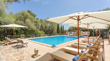 Uma área à beira da piscina com espreguiçadeiras e guarda-sóis, cercada por vegetação.
