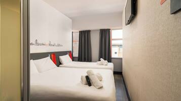 Quarto de hotel com duas camas, uma obra de arte urbana na parede, televisão de tela plana e uma janela com cortinas.