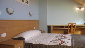 Quarto com cama de madeira, escrivaninha e cadeira. Há uma prateleira na parede e um quadro emoldurado acima da cama.