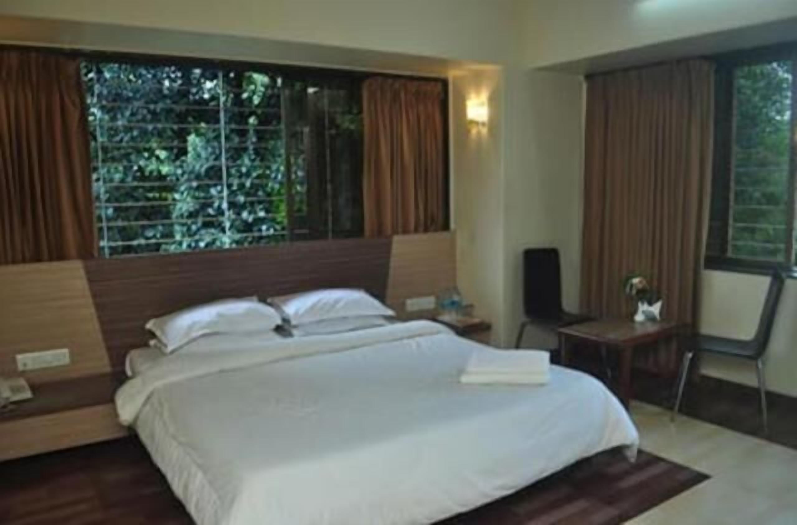 Quarto de hotel com uma cama grande, uma escrivaninha com cadeira e uma janela com cortinas.