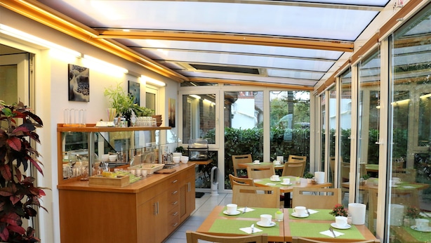 Cozinha moderna com estrutura de vidro, mobiliário de madeira e área de jantar com mesas preparadas para quatro pessoas.