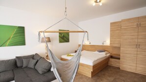Quarto moderno com cama em rede, sofá cinza, guarda-roupa de madeira e pintura de folha verde.