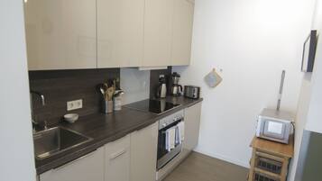 Uma cozinha moderna com bancada escura, eletrodomésticos de aço inoxidável e um micro-ondas sobre um suporte de madeira.
