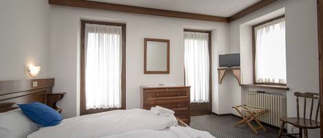 Quarto de hotel com cama, cómoda, cadeira, televisão e janela com cortinas.