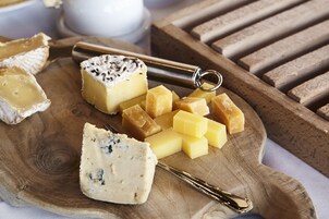Uma tábua de madeira com vários queijos e uma faca para queijo.