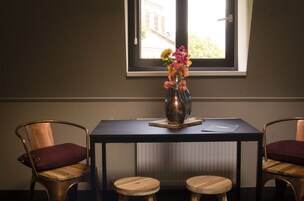Uma área de refeições com uma mesa, duas cadeiras, um vaso com flores e uma janela com vista.