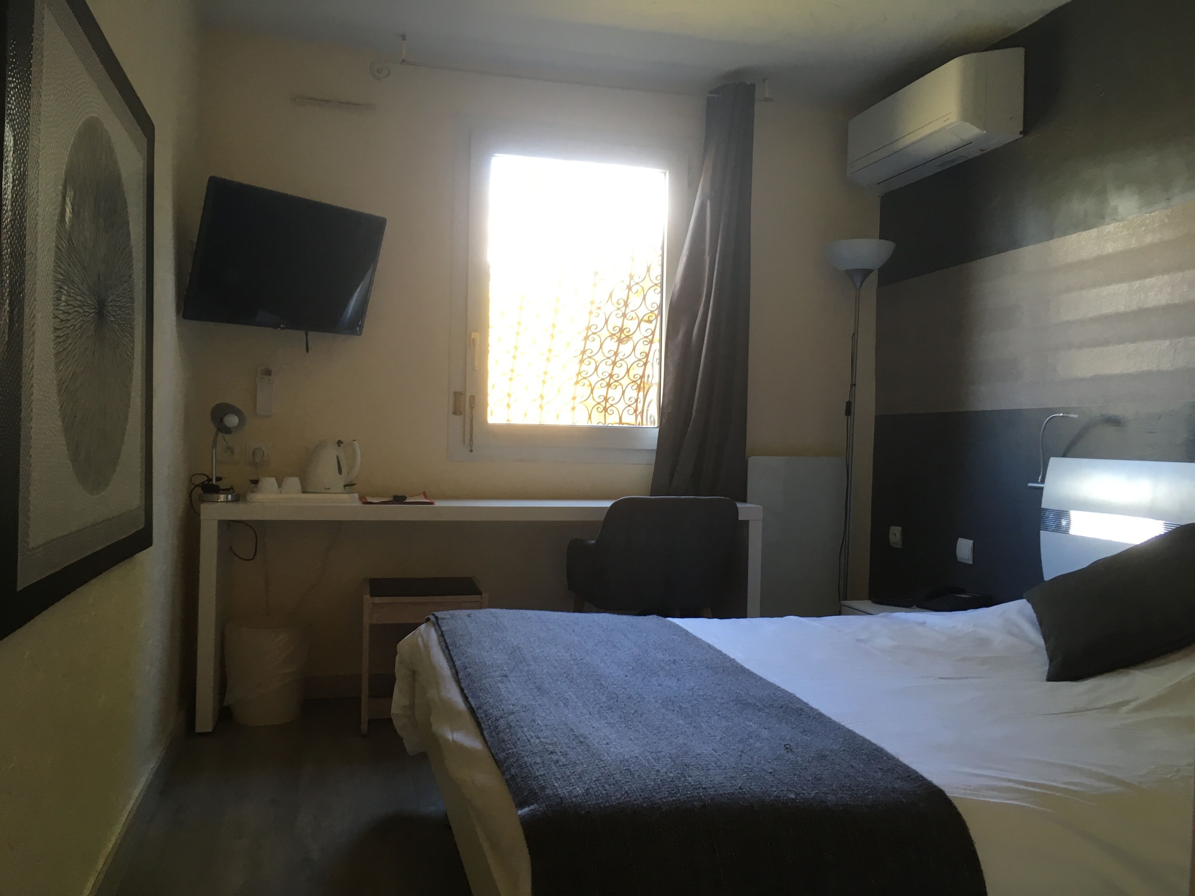 Quarto de hotel com cama, escrivaninha, cadeira, televisão e ar condicionado.