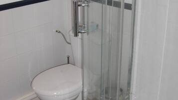 Casa de banho com sanita, cabine de duche em vidro e tapete de banho azul.