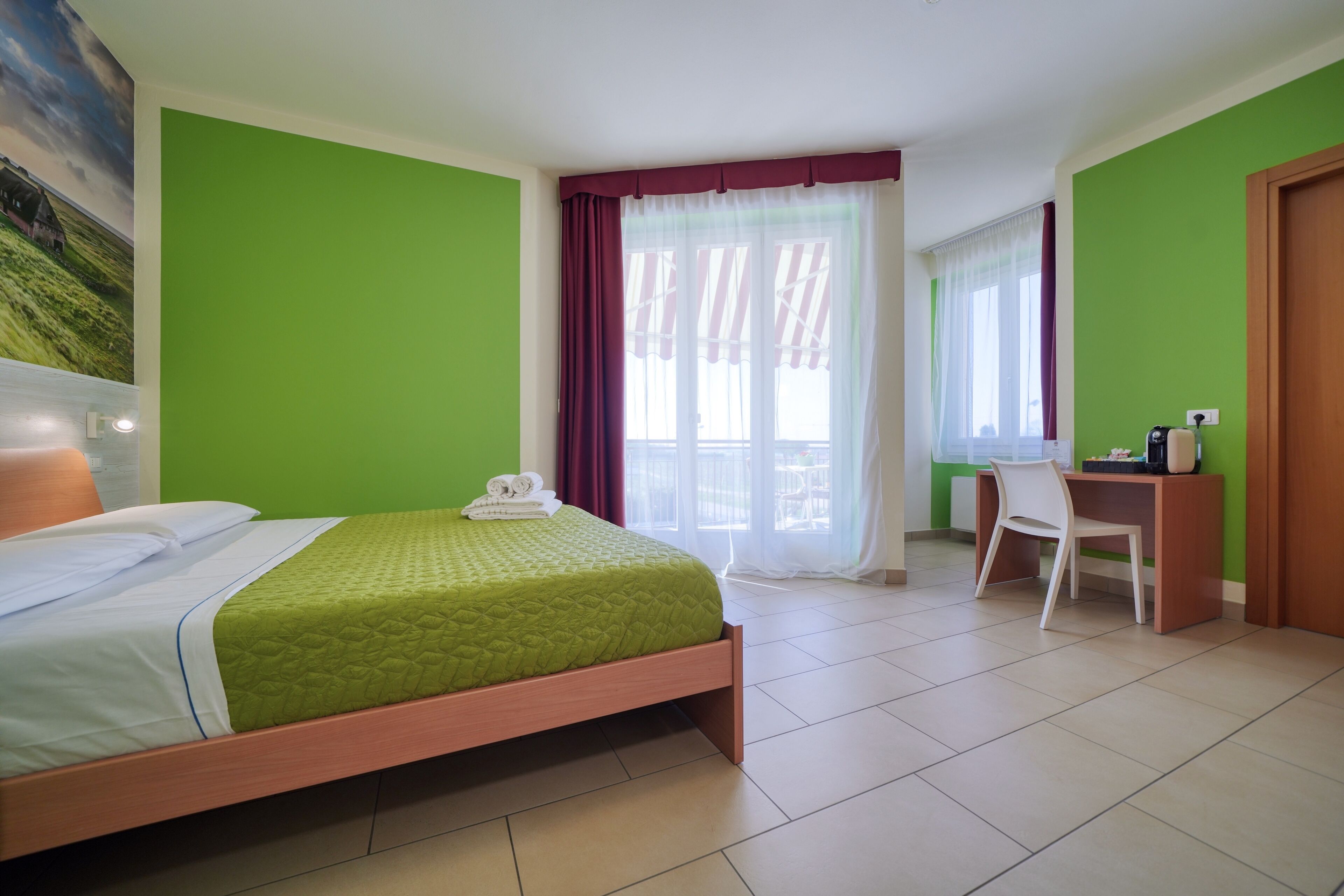 Quarto de hotel com cama, escrivaninha, cadeira e janela com cortinas.