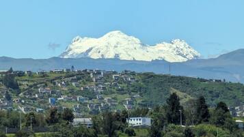 Uma montanha com picos nevados ao fundo, uma cidade com vários edifícios em primeiro plano e um céu azul claro acima.