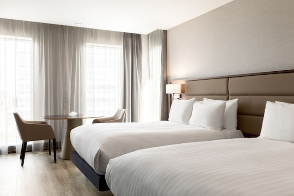 Quarto de hotel com duas camas, uma escrivaninha e uma cadeira.