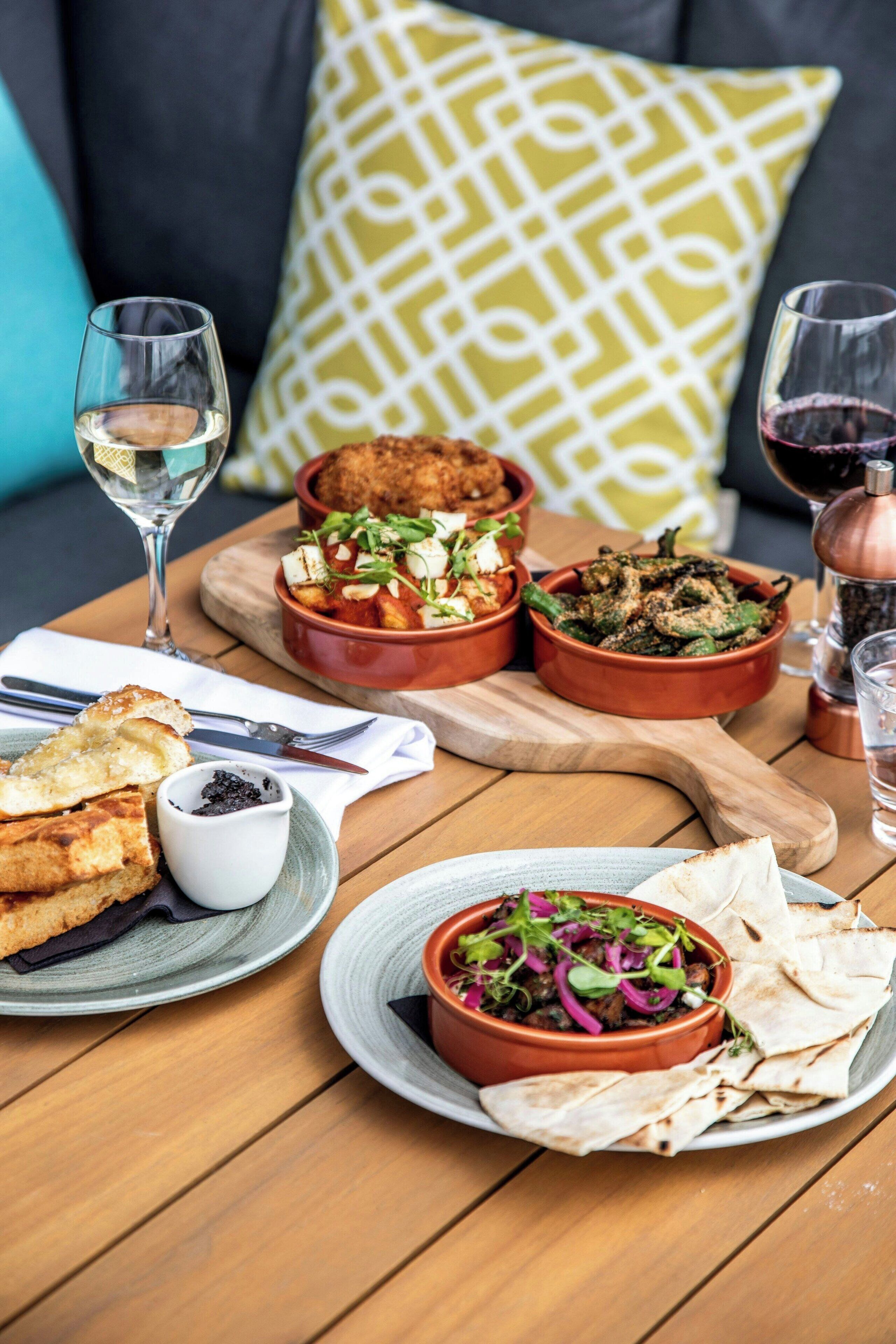 Uma mesa de madeira com diversos pratos, incluindo pão, uma salada e legumes assados.