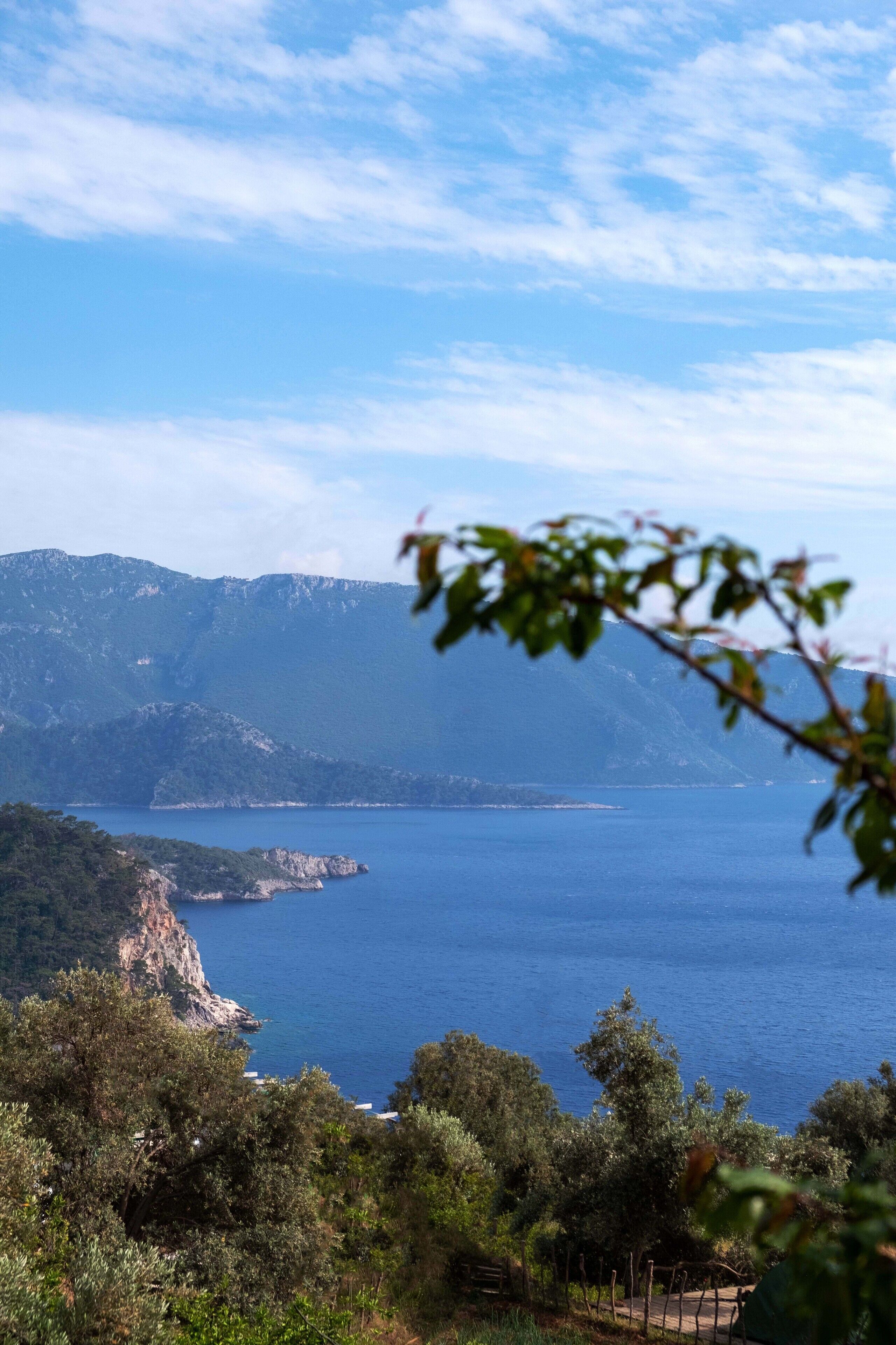 Paisagem costeira com vista clara para o mar, montanhas e vegetação.