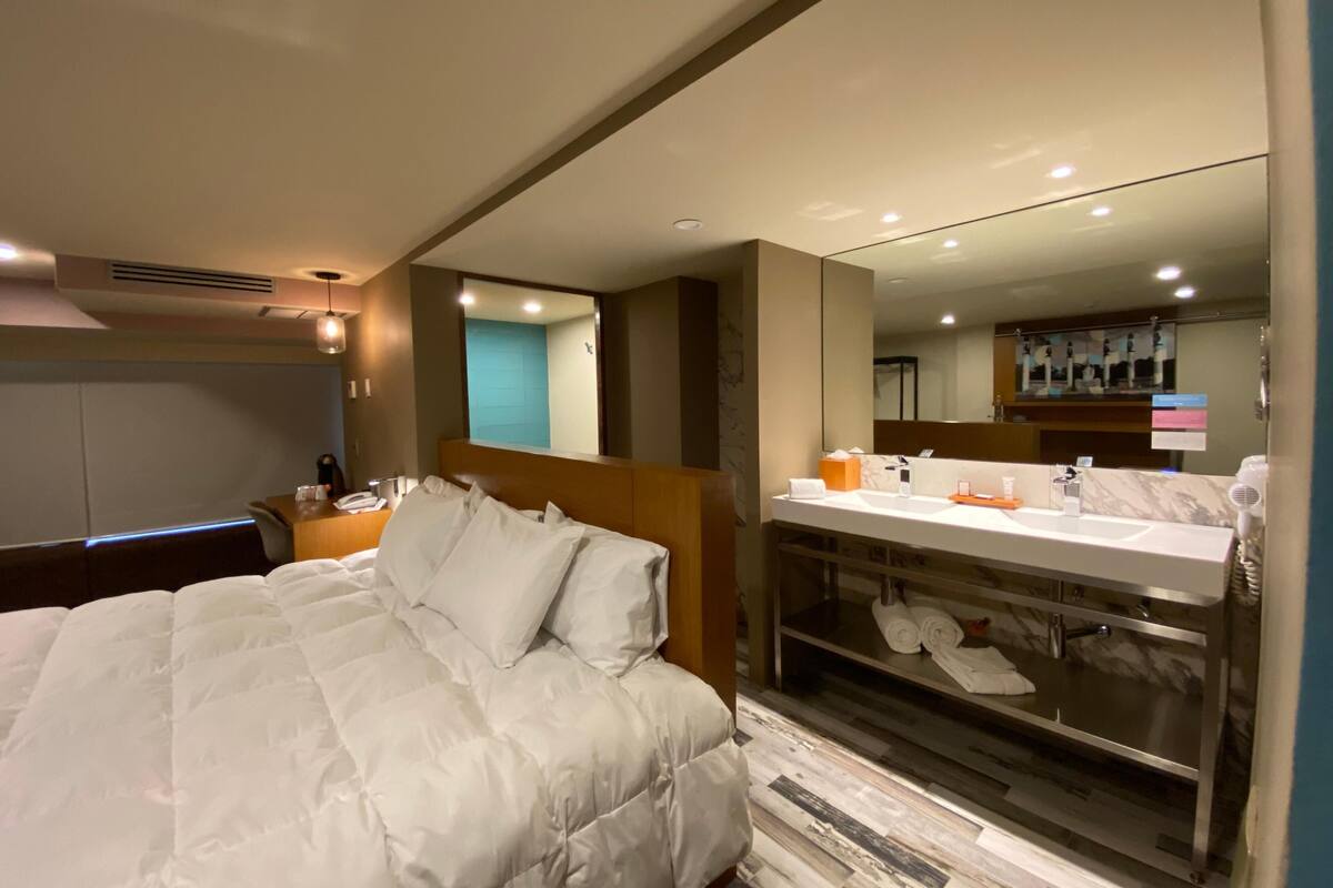 Quarto de hotel com cama, banheiro com espelho e pia.