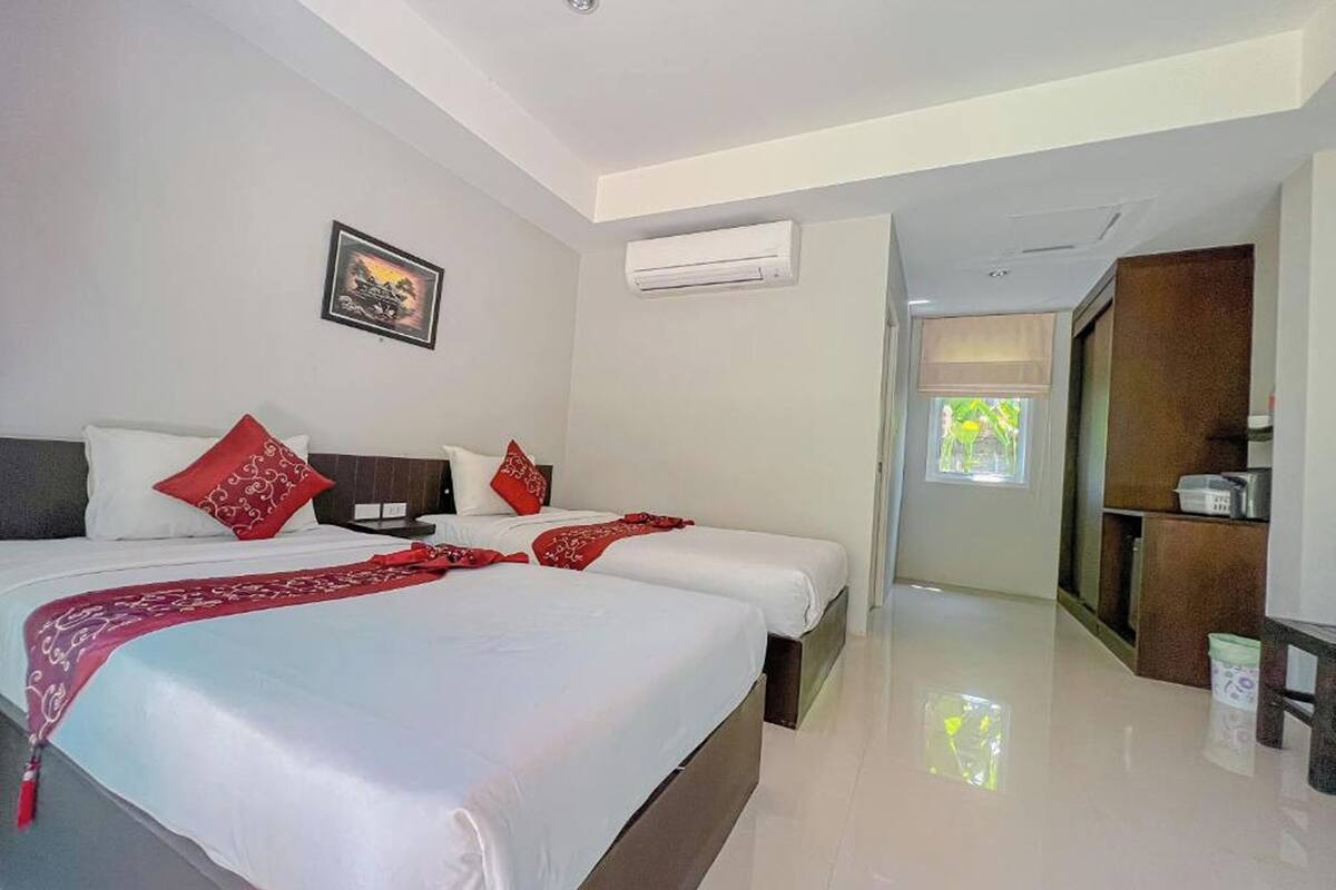 Quarto de hotel com duas camas, uma janela grande, aparelho de ar condicionado e vista para o exterior.