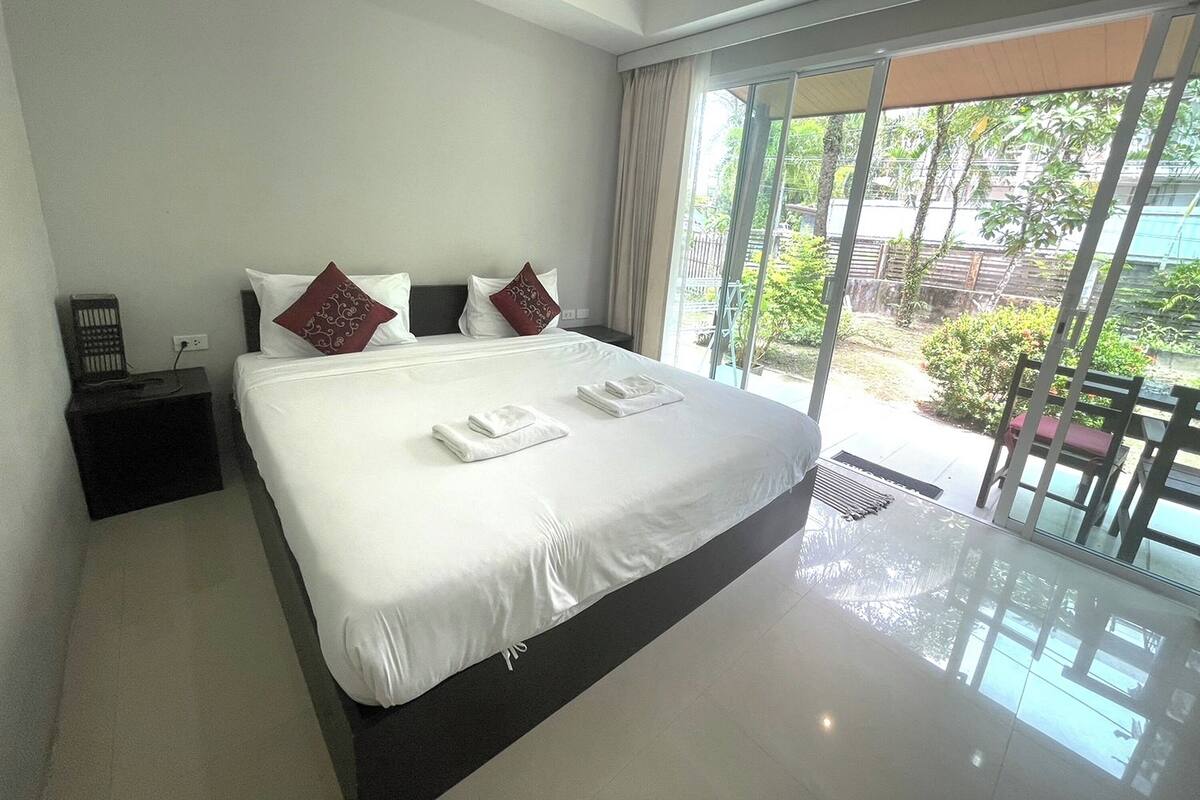 Quarto de hotel moderno com uma cama grande, roupa de cama branca e duas almofadas decorativas.