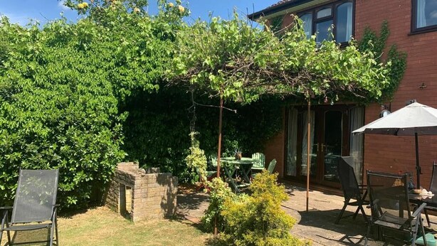 Um quintal com pérgola, muro de tijolos, arbusto pequeno e móveis de exterior.