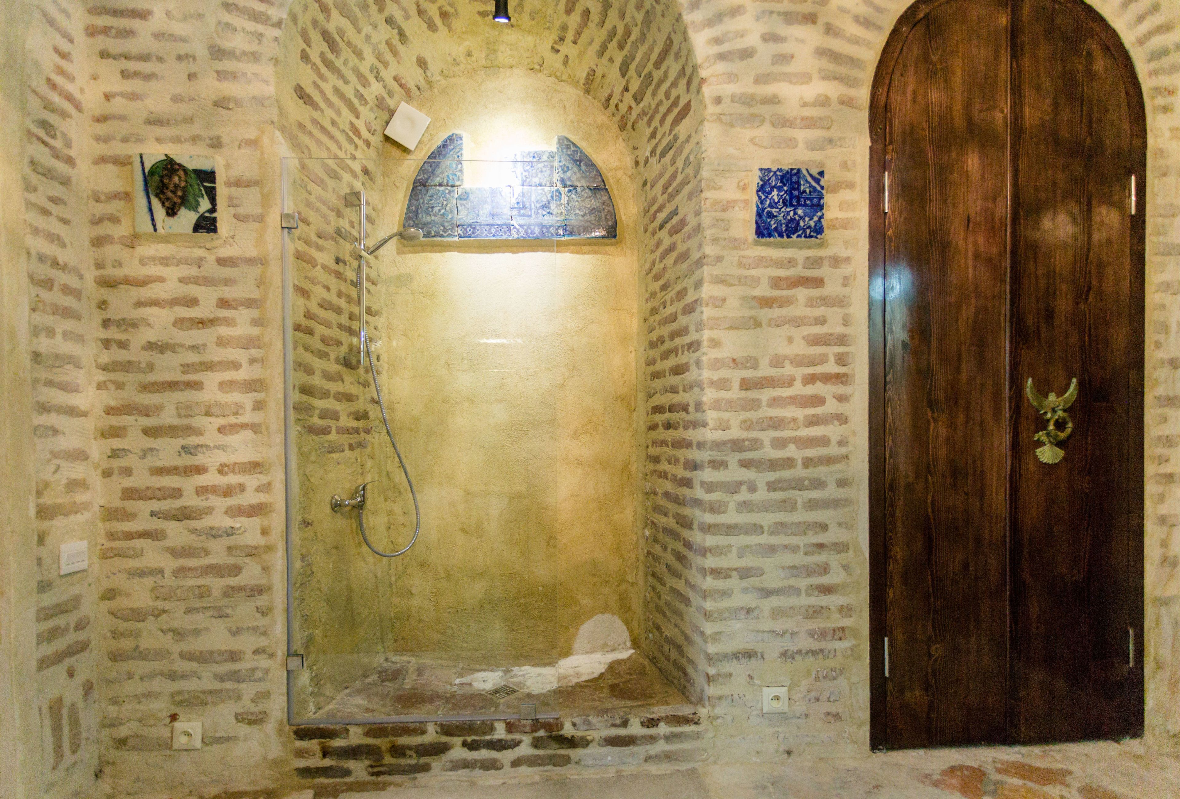Chuveiro com porta de vidro, porta de madeira e parede de tijolos.