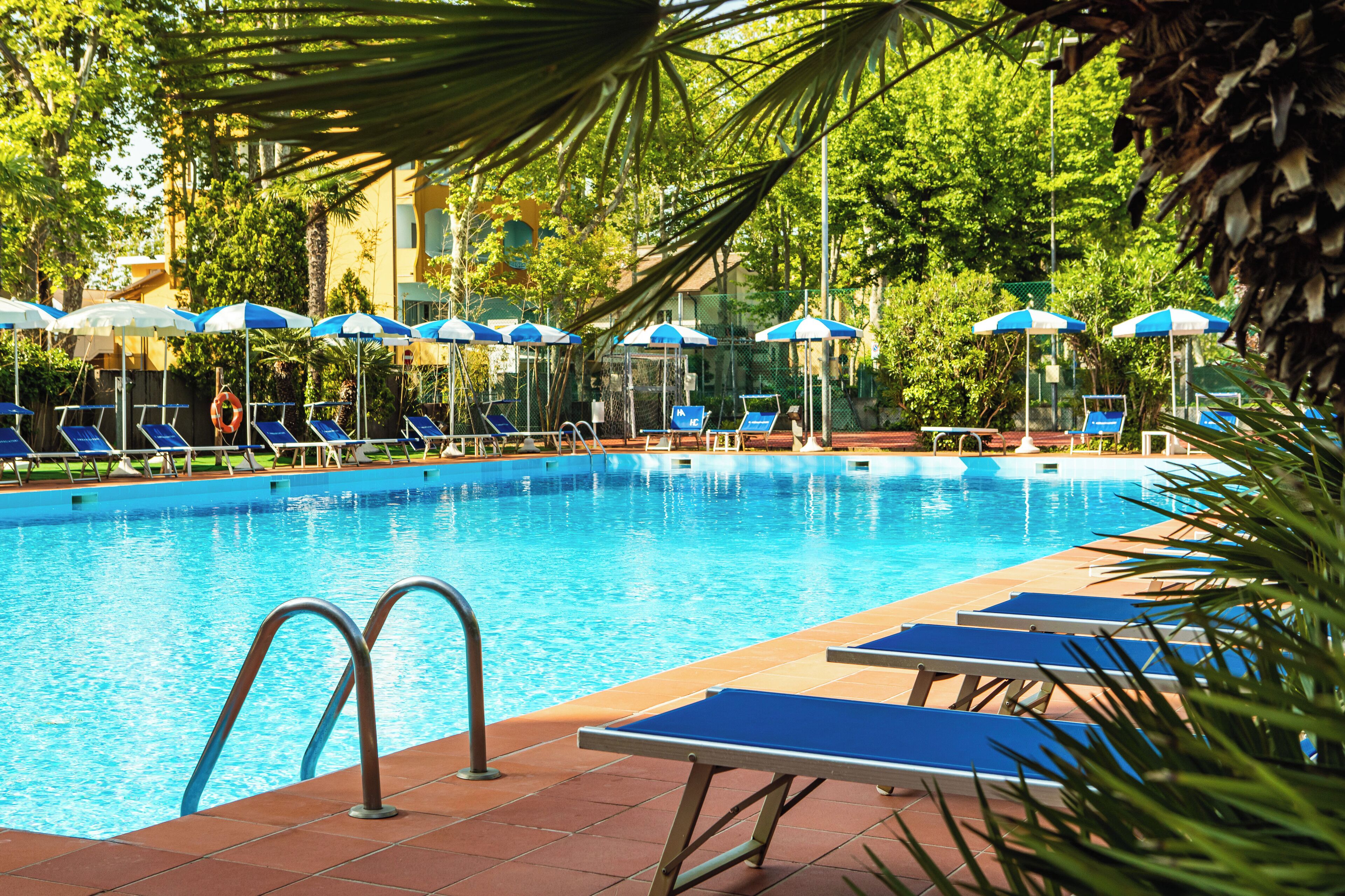 Piscina com cadeiras de sol azuis e guarda-sóis, rodeada por árvores.